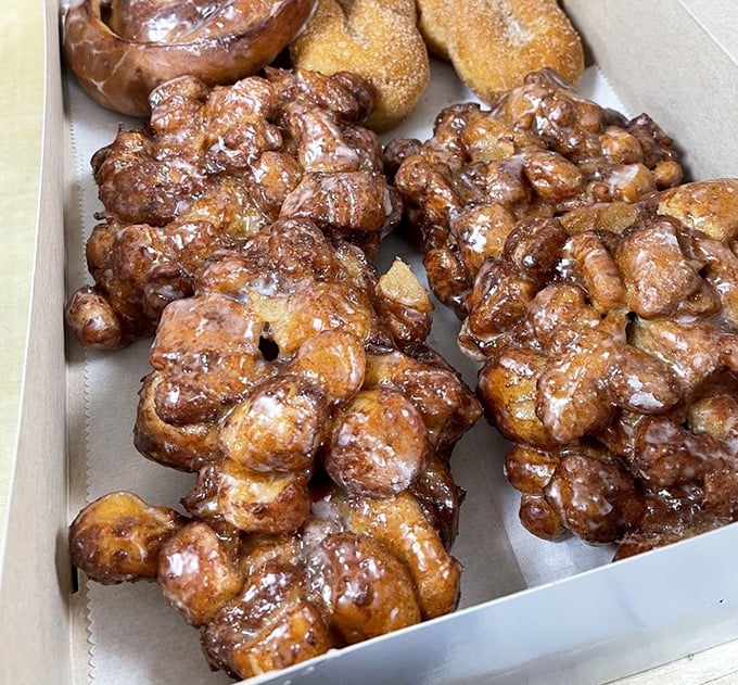 Behold the apple fritters in their natural habitat – gloriously misshapen, glistening with glaze, and absolutely unapologetic about their caloric content.