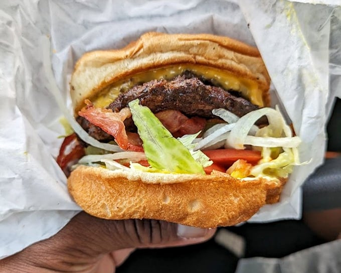 Behold the bacon cheeseburger in its natural habitat—wrapped in paper, bursting with toppings, and destined to make your car smell heavenly.
