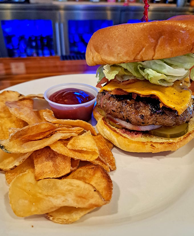 Behold burger perfection—a towering masterpiece of beef, cheese, and fresh toppings alongside homemade chips that shatter with each satisfying crunch.