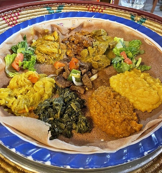 Behold the Ethiopian combination platter—a colorful canvas of flavors atop injera bread. It's like edible art where every brushstroke is deliciously spiced.
