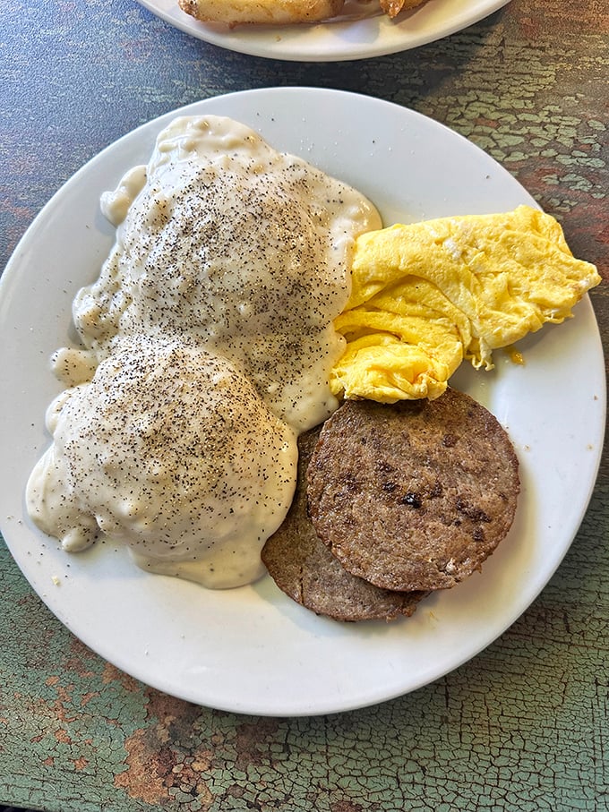 Behold the star attraction: biscuits smothered in pepper-flecked gravy alongside golden eggs and sausage. Breakfast nirvana on a humble white plate.