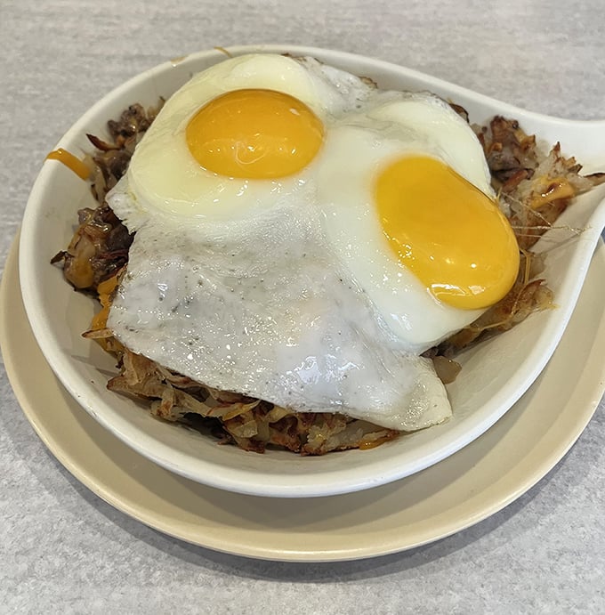Sunny-side up eggs perched atop a mountain of hash browns – breakfast architecture that would make Frank Lloyd Wright weep with joy.