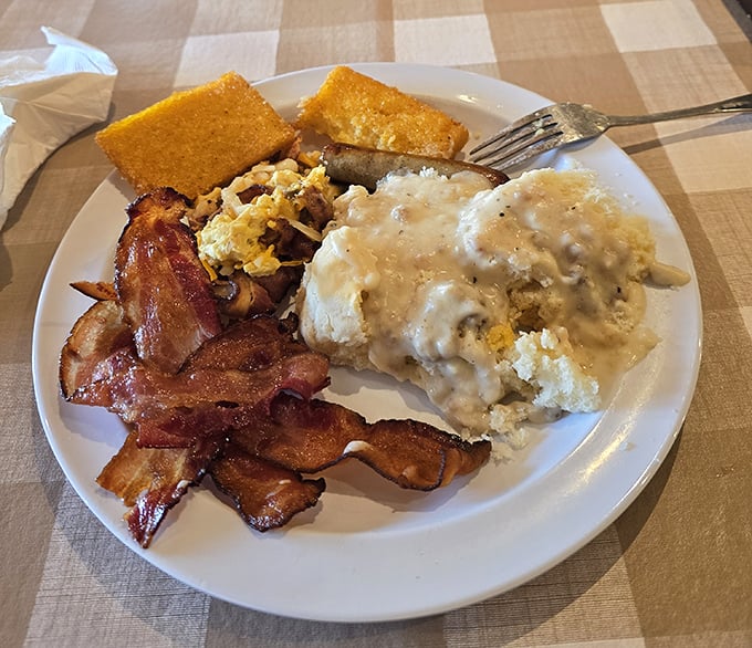 Behold the breakfast of champions! Crispy bacon, cornbread, and eggs smothered in sausage gravy—a plate that says "diet starts tomorrow."