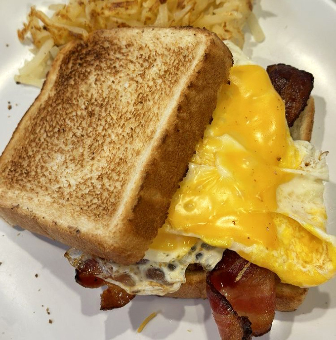 Breakfast architecture at its finest—perfectly toasted bread supporting a glorious stack of egg, cheese, and bacon. The home fries are just showing off.