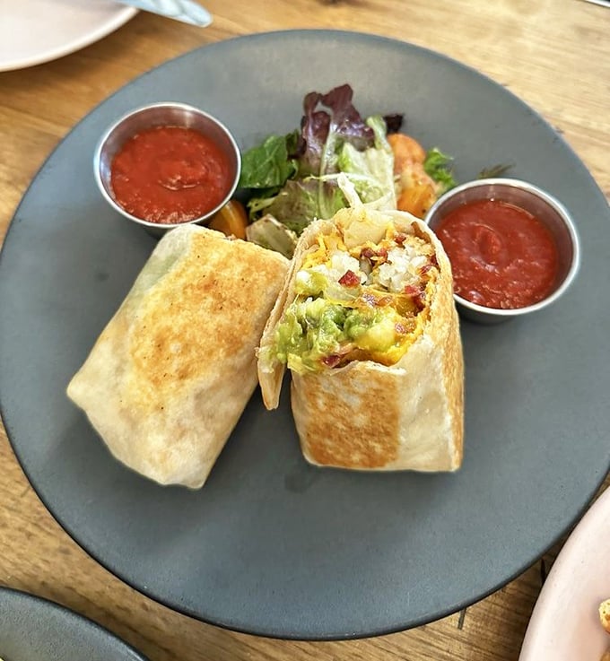 The breakfast burrito in its natural habitat – perfectly grilled, generously stuffed, and flanked by salsa roja that's practically begging to join the party.