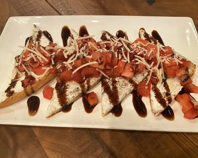 This bruschetta isn't just appetizer – it's edible art. Crisp bread, creamy cheese, fresh tomatoes, and that balsamic drizzle you'd happily drink straight.