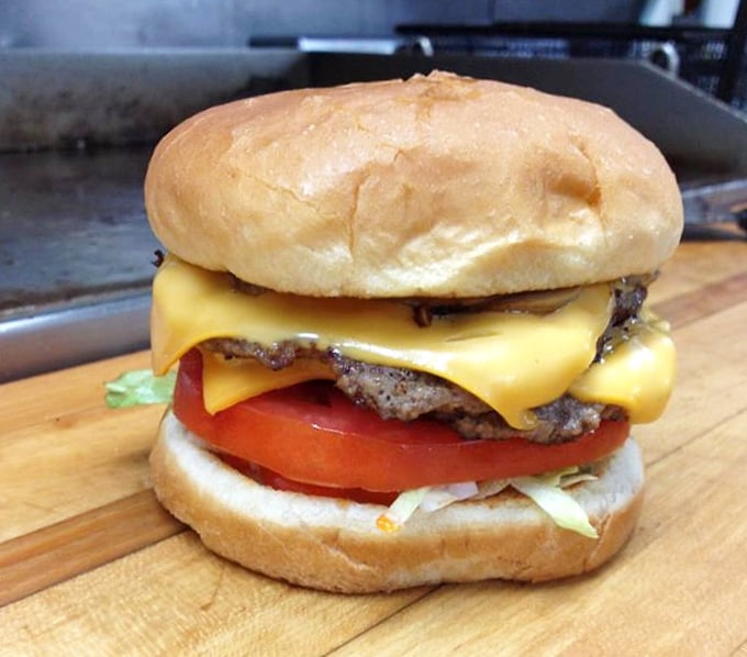 Behold the cheeseburger in its natural habitat – perfectly melted American cheese cascading over a hand-formed patty with garden-fresh toppings.