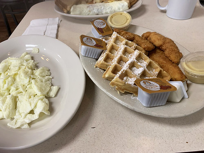 Behold the star attraction: golden-fried chicken alongside a perfectly formed waffle, dusted with powdered sugar—a sweet and savory symphony.