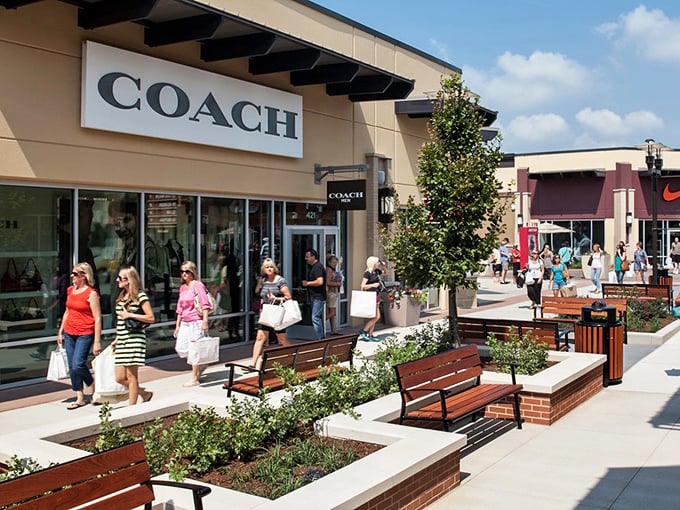 Coach's elegant storefront sits amid thoughtfully designed landscaping. Those benches aren't just decorative—they're relationship savers during marathon shopping sessions.