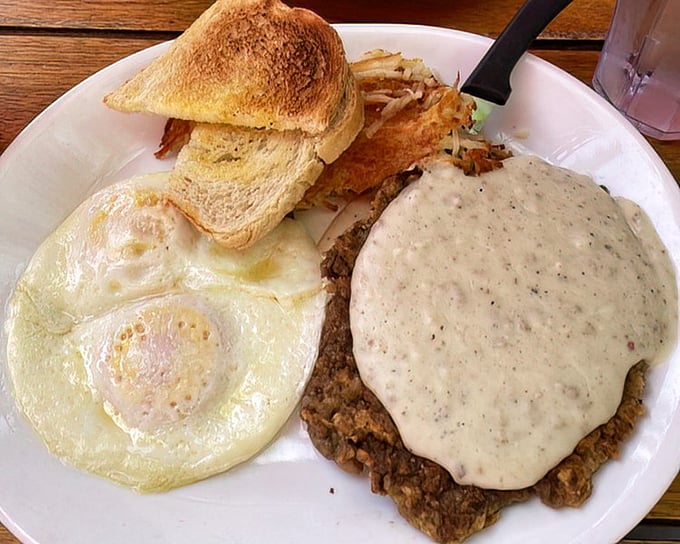 The holy trinity of breakfast perfection: golden-crisp country fried steak smothered in pepper gravy, a sunny-side-up egg, and hash browns that demand respect.