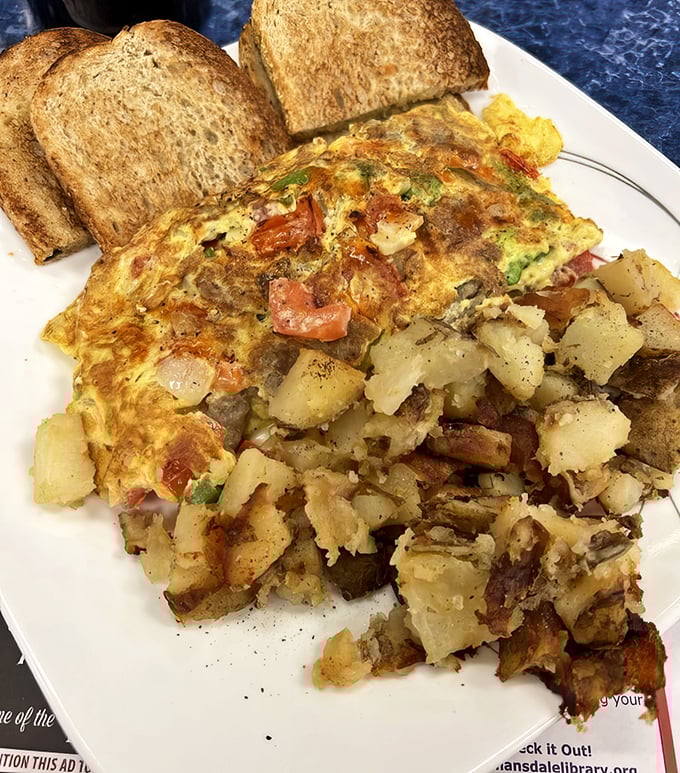 Behold the omelet in its natural habitat—perfectly folded, generously stuffed, and flanked by home fries that deserve their own zip code.