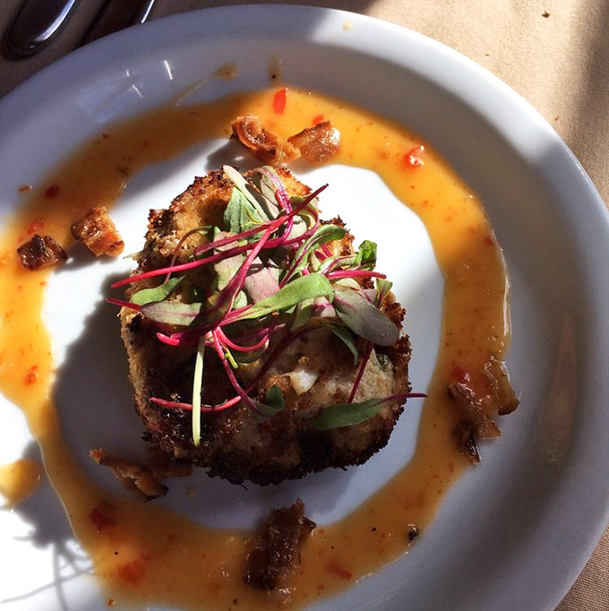 The crab cake arrives like a golden crown, perfectly seared and surrounded by a moat of sauce you'll want to swim in.