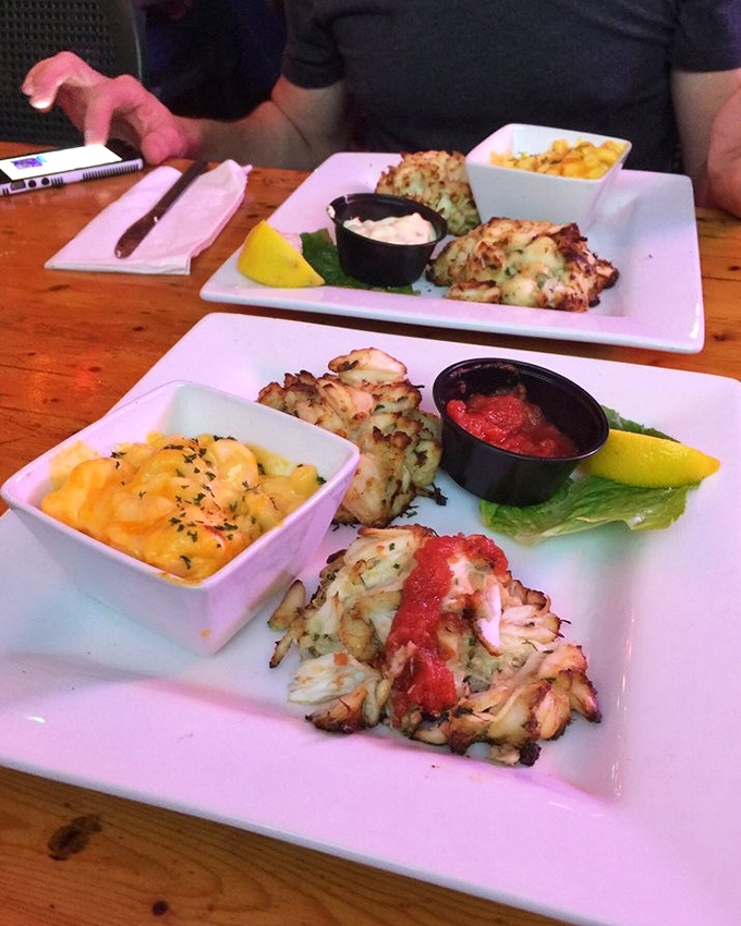 Not all heroes wear capes—some come on white plates with mac and cheese, perfectly golden exteriors hiding treasures of sweet jumbo lump crab.