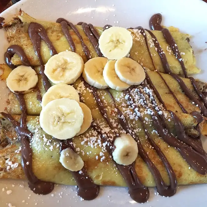 Chocolate drizzles dance across golden crepes while banana slices stand at attention. This isn't breakfast – it's edible architecture with a side of joy.