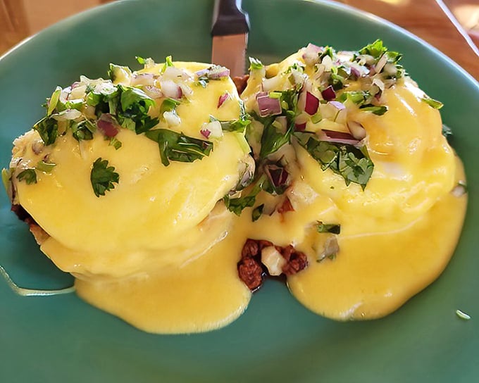 Hollandaise cascades over perfectly poached eggs like a sunrise-colored waterfall, garnished with fresh herbs that add both color and zing.