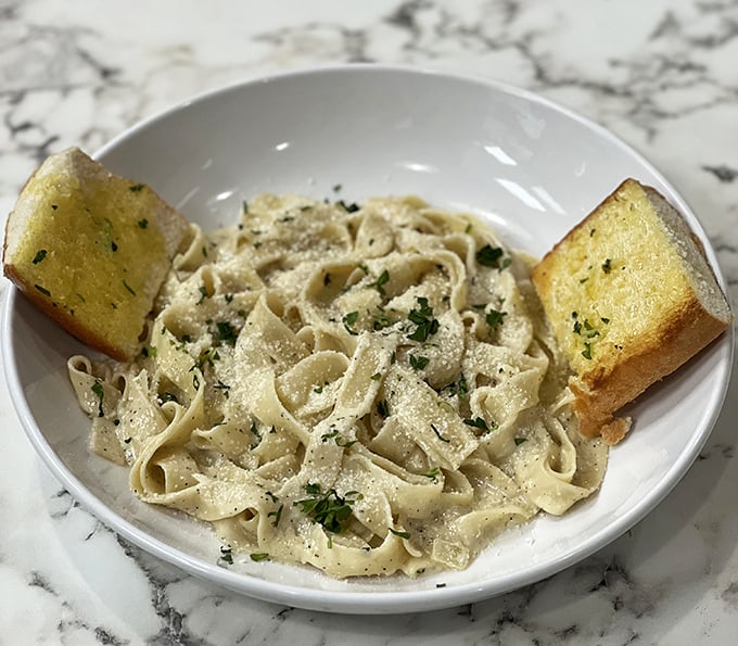 Fettuccine Alfredo so creamy it should come with a warning label. Those garlic bread bookends aren't just accessories – they're sauce-sopping necessities.