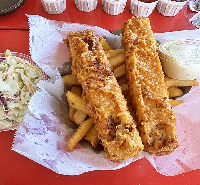 Golden-battered fish fillets resting on a bed of fries with coleslaw standing by. This isn't just fish and chips – it's edible sunshine.