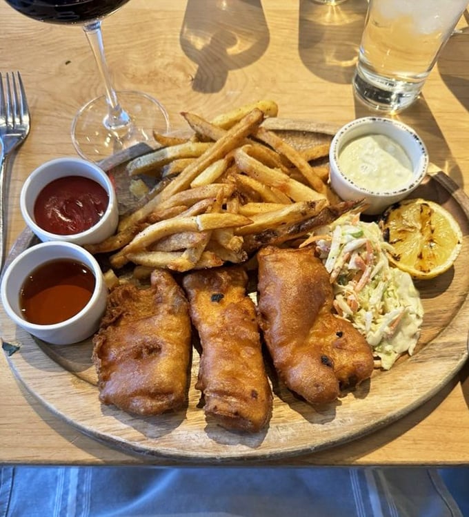Golden-battered Atlantic cod that shatters with each bite, alongside chips that somehow defy the laws of potato physics by staying crisp till the last fry.