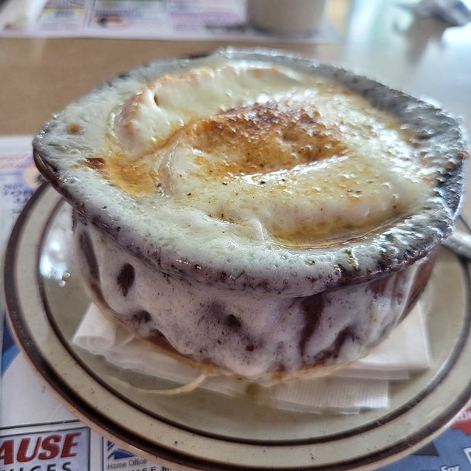 This French onion soup isn't just topped with cheese – it's wearing a magnificent crown that would make Louis XIV weep with envy.
