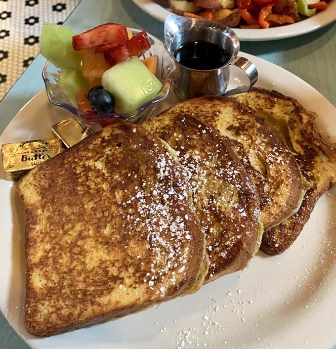 Golden-brown French toast dusted with powdered sugar—this isn't breakfast, it's edible artwork with a side of fresh fruit.