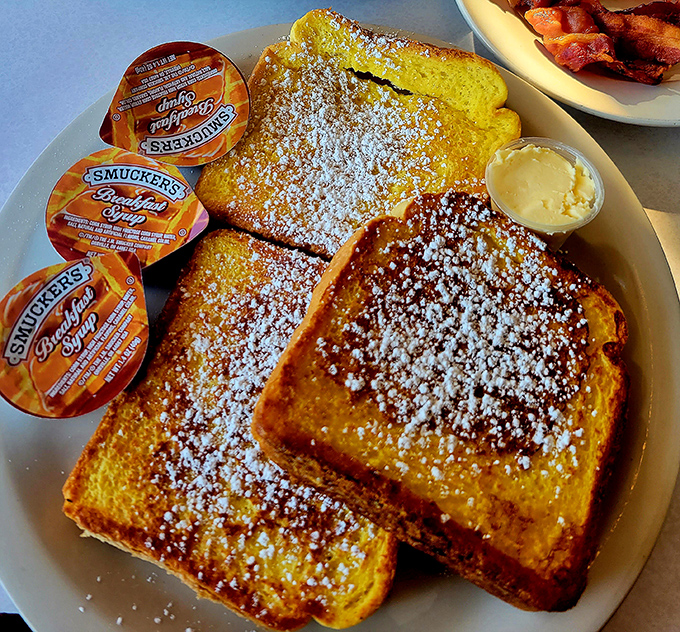 The French toast arrives like a golden revelation—perfectly crisp exterior giving way to custardy interior, with powdered sugar falling like the gentlest snowfall.