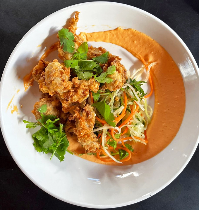 Golden-fried oysters lounging in a vibrant orange sauce with fresh herbs—like little crispy treasures that make you wonder why you'd eat oysters any other way.