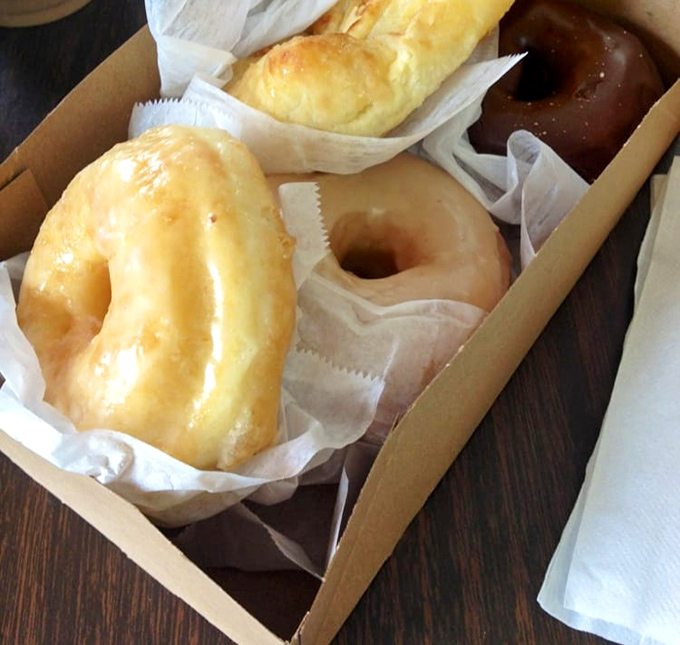 Behold the holy grail of glazed perfection—each one glistening like edible sunshine in a brown paper treasure chest.