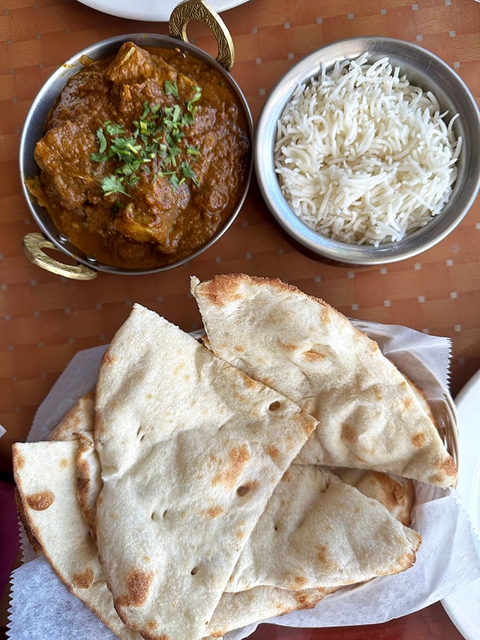 The legendary goat curry arrives in all its glory – tender meat swimming in a complex sauce that's been simmered to perfection, alongside fluffy basmati rice and fresh naan.