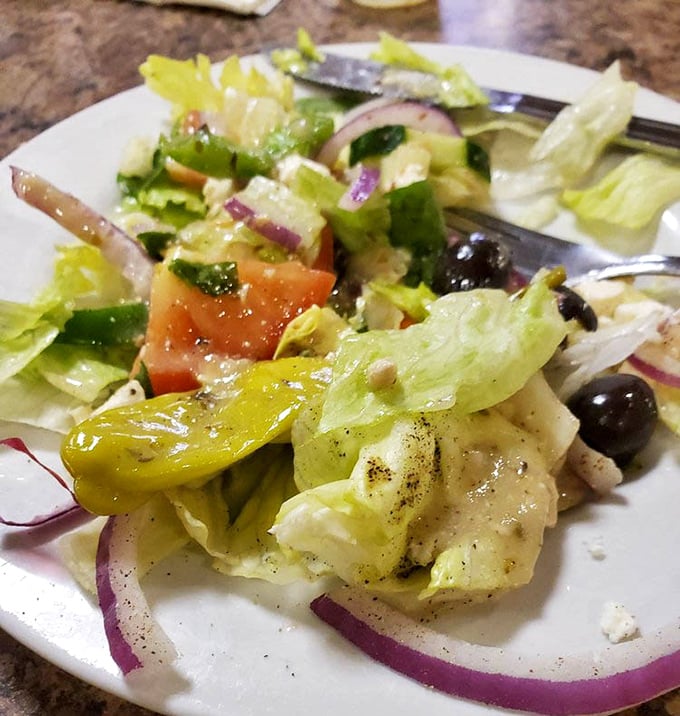 The Greek salad in all its glory – crisp lettuce, vibrant tomatoes, purple onions, and olives playing supporting roles to the star: chunks of authentic feta.