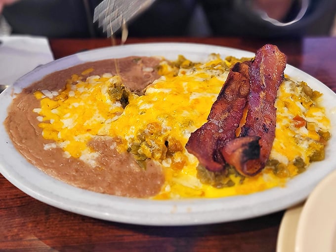 Breakfast nirvana achieved: eggs draped in green chile sauce with melted cheese and bacon standing at attention. This plate doesn't just break your fast—it demolishes it with flavor.