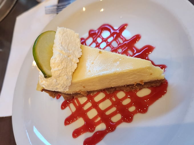 The legendary key lime pie arrives like a celebrity – perfectly tart-sweet filling, buttery graham cracker crust, and that artistic raspberry drizzle.