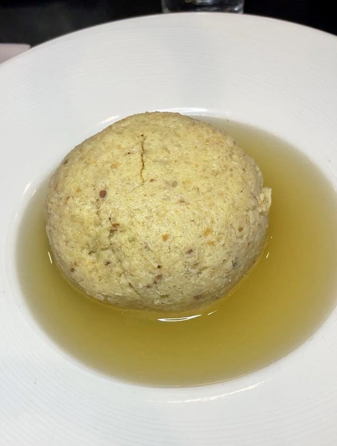 Behold, the star of the show—a perfect matzo ball floating majestically in golden broth. Jewish penicillin at its finest, no prescription needed.