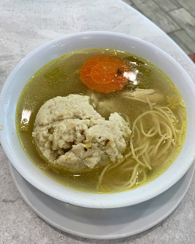 Behold the star attraction—matzo ball soup that would make your grandmother weep with joy, floating in broth clear enough to read through.