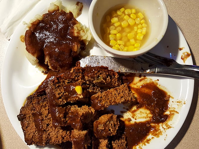 Behold the legendary meatloaf in all its glory – thick slices bathed in rich gravy alongside mashed potatoes and corn. Grandma would approve, then ask for the recipe.
