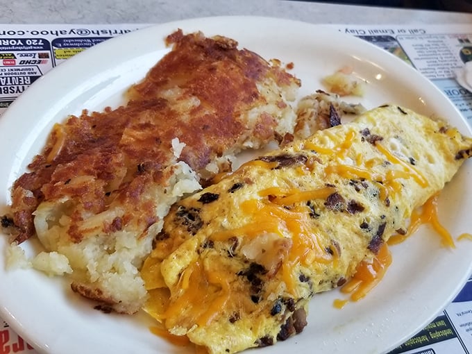 Behold the omelet in its natural habitat—fluffy, cheese-laden, and perfectly paired with home fries that deserve their own fan club.