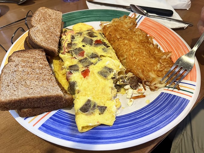 A properly executed omelet is culinary poetry—this one tells a story of perfectly cooked eggs embracing savory fillings alongside crispy hash browns.