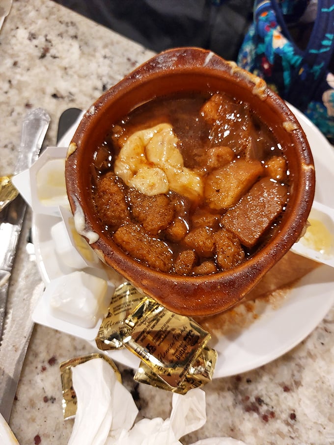 Behold the legendary French onion soup in its natural habitat—a ceramic crock filled with savory broth, tender bread, and enough melted cheese to make a cardiologist wince.