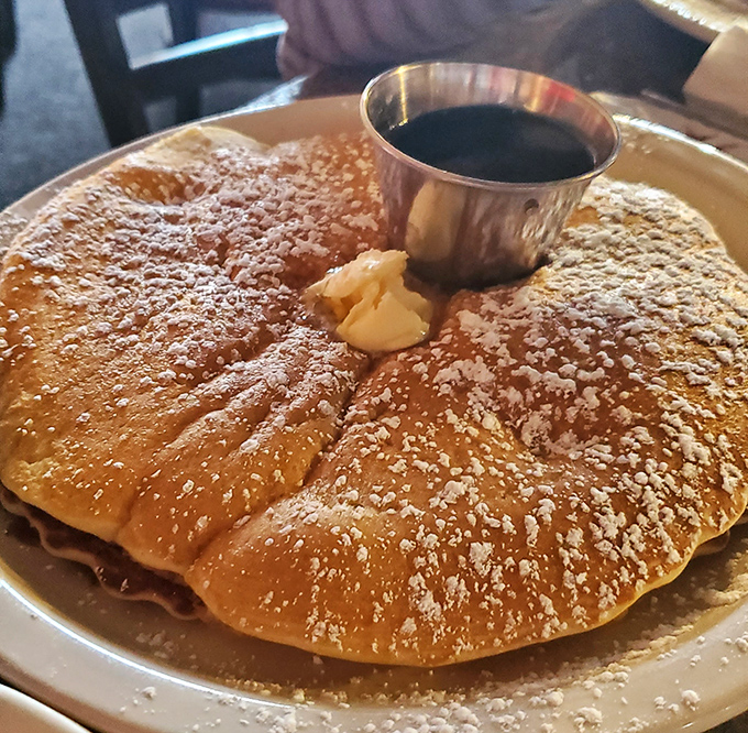 This golden pancake, dusted with powdered sugar and crowned with a pat of butter, isn't just breakfast—it's edible sunshine on a plate.