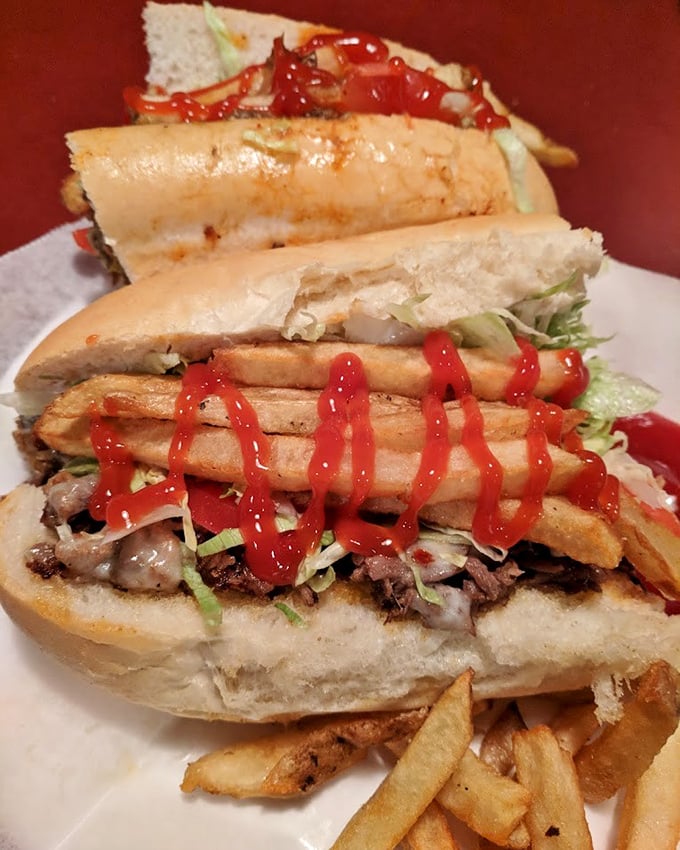 Sandwich architecture at its finest—layers of thinly sliced steak, melted cheese, and fresh toppings create a masterpiece that demands both hands and zero shame.