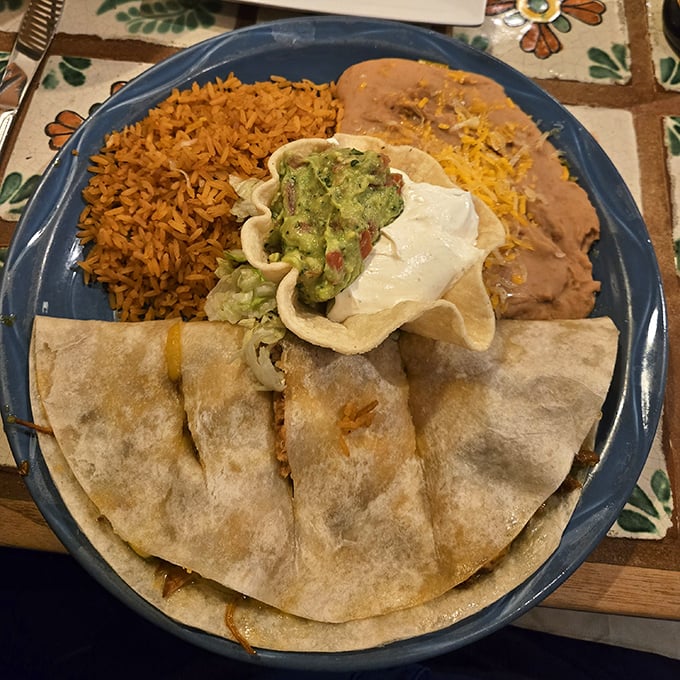 Behold the quesadilla in its natural habitat—surrounded by Mexican rice, refried beans, and a dollop of guacamole that deserves its own Instagram account.