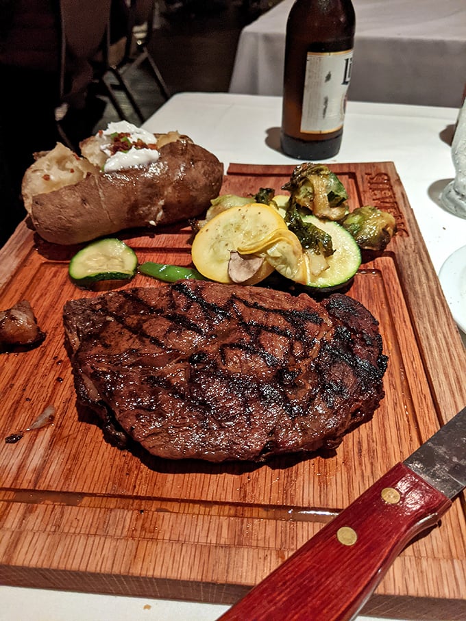 A perfectly seared ribeye shares the stage with a loaded baked potato and seasonal vegetables. This wooden board presentation deserves a standing ovation!