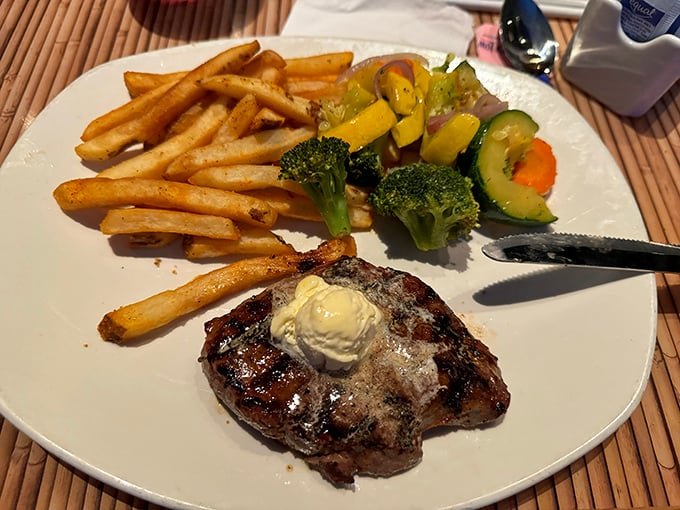 A perfectly seared steak arrives with a dollop of butter slowly melting into meaty paradise, flanked by golden fries and vibrant vegetables.