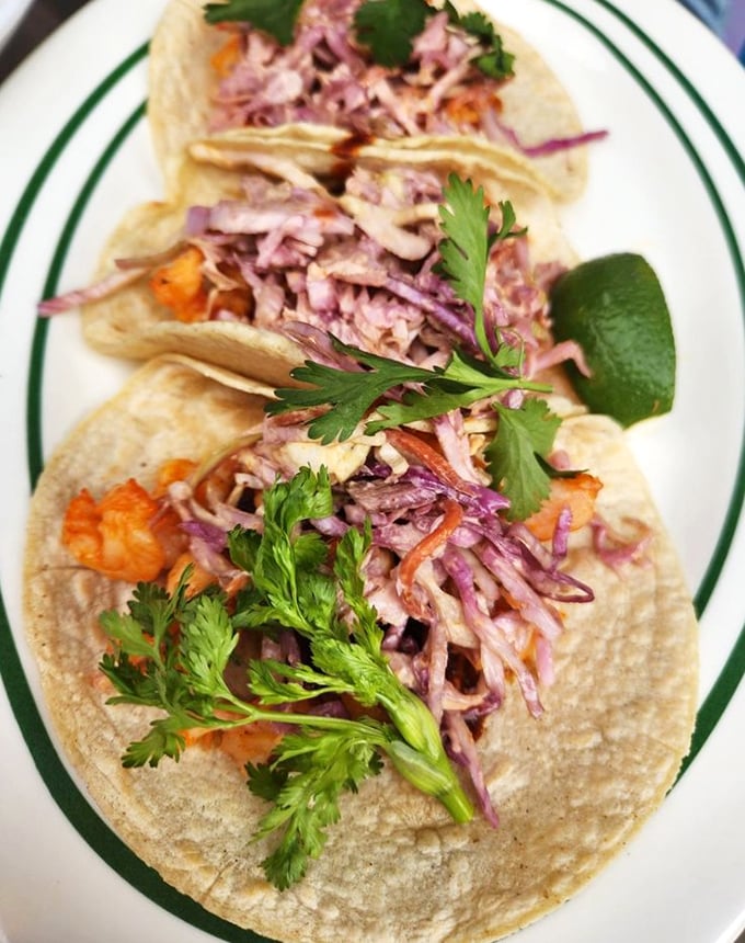 These shrimp tacos arrive dressed to impress – purple cabbage confetti and cilantro crowns making each bite a celebration.