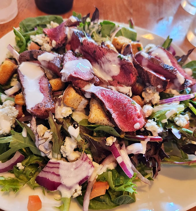 The legendary Black & Blue Steak Salad arrives like edible artwork—perfectly seared beef resting atop fresh greens with blue cheese crumbles playing hide-and-seek throughout.