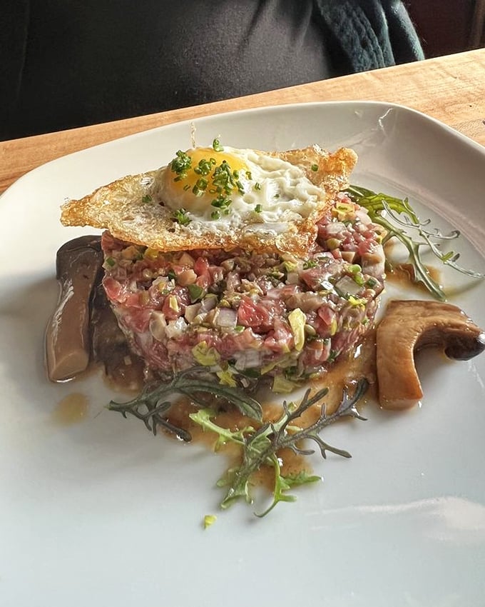 Behold the steak tartare that launched a thousand food pilgrimages – crowned with a perfect egg, surrounded by mushrooms that practically genuflect in its presence.