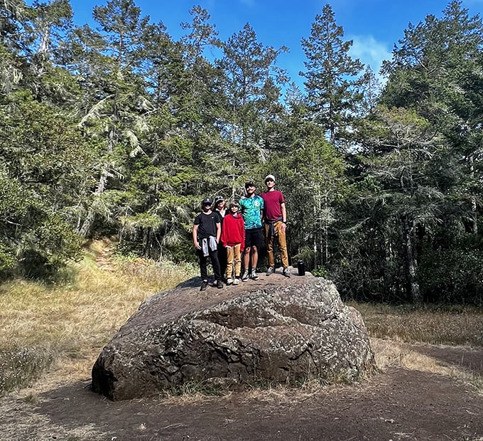 A family celebrates their summit conquest atop a trail boulder—the universal "we made it" pose that's mandatory in hiking circles.