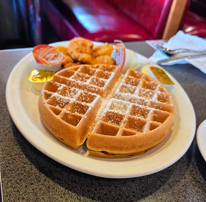 Golden waffle perfection with a dusting of powdered sugar—the grid pattern practically engineered to hold maximum syrup.