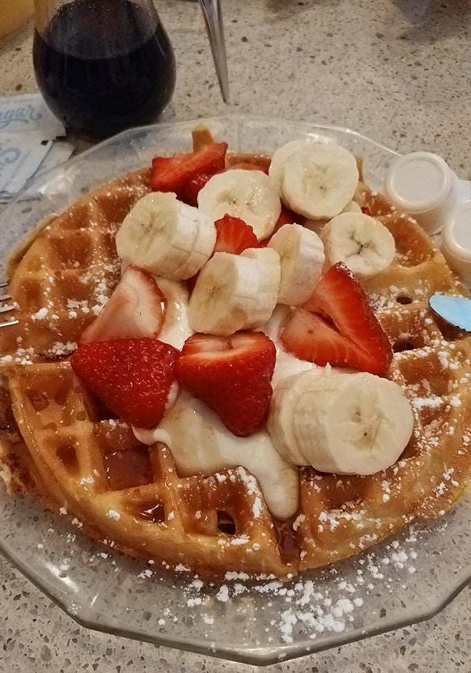 Behold the Belgian waffle in its natural habitat, adorned with fresh fruit and powdered sugar like it's dressed for the breakfast prom.