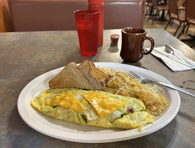 This Western omelet isn't trying to impress Instagram—it's too busy delivering cheese-draped satisfaction alongside a mountain of hash browns that means business.
