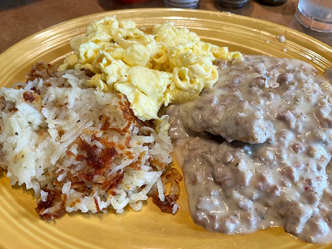 Behold the holy trinity of breakfast: creamy sausage gravy, golden hash browns, and fluffy scrambled eggs—a plate that whispers, "Good morning, beautiful."